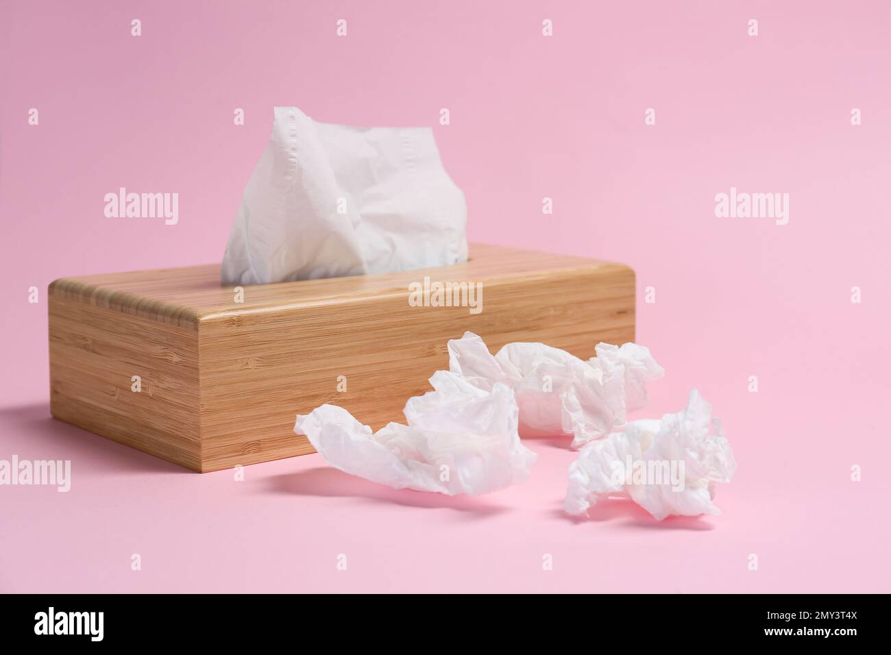 Holder with paper tissues and used crumpled napkins on pink background ...
