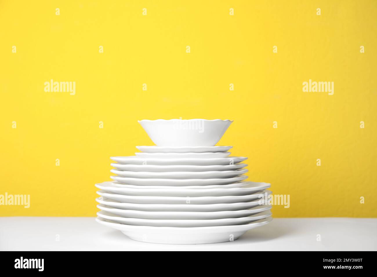 Stack of clean plates on white table against yellow background Stock ...