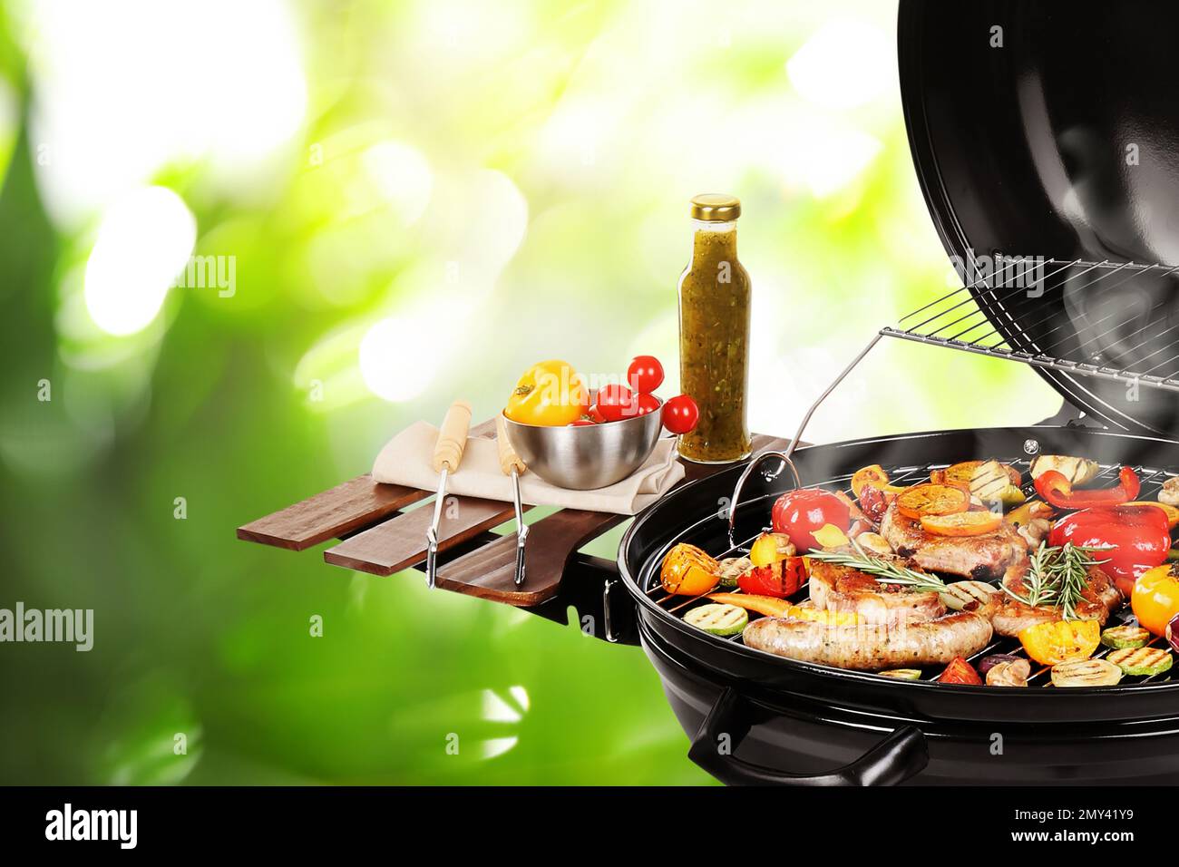 Barbecue grill with meat products and vegetables on blurred green ...