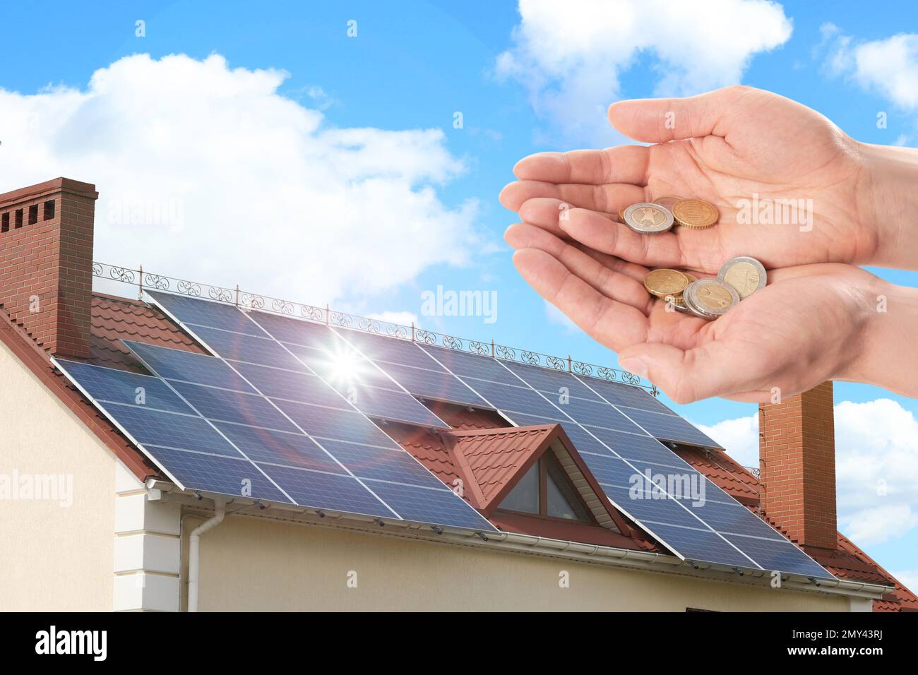 Man holding coins against house with installed solar panels. Renewable ...