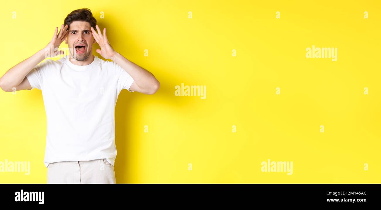 Frustrated guy looking alarmed, holding hands on head and feeling ...
