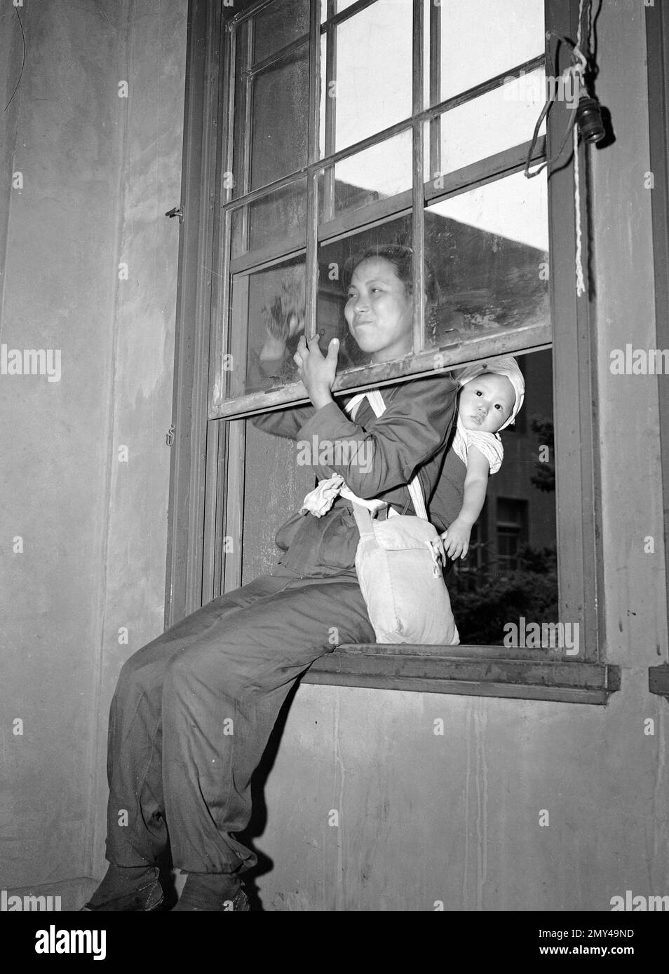 A Japanese mother with a baby strapped to her back cleans a window at ...