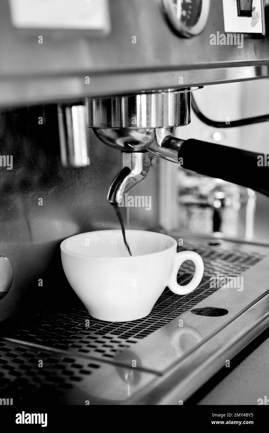 A vertical grayscale of coffee pouring from the coffee machine into a ...