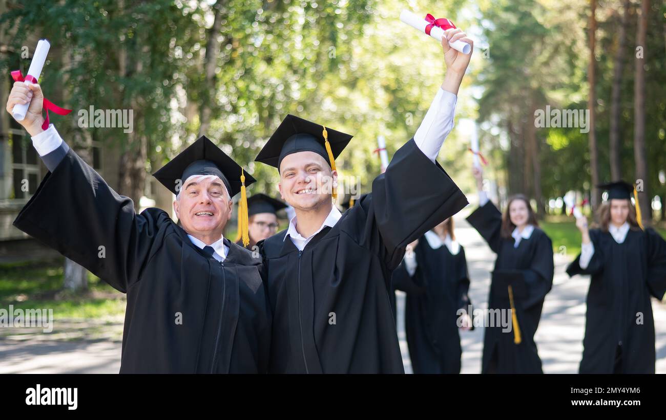 A group of graduates in robes outdoors. An elderly man and a young guy ...