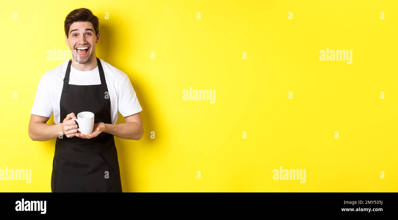 Happy barista in black apron holding coffee cup, laughing and standing ...