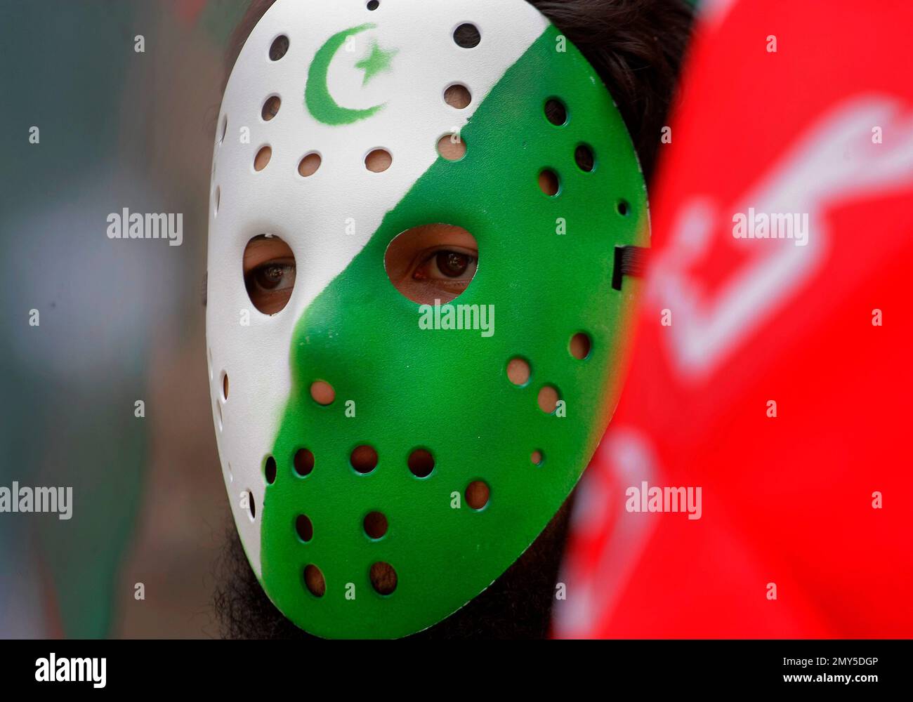 A Pakistani vendor wears a mask painted with the colors of the national ...