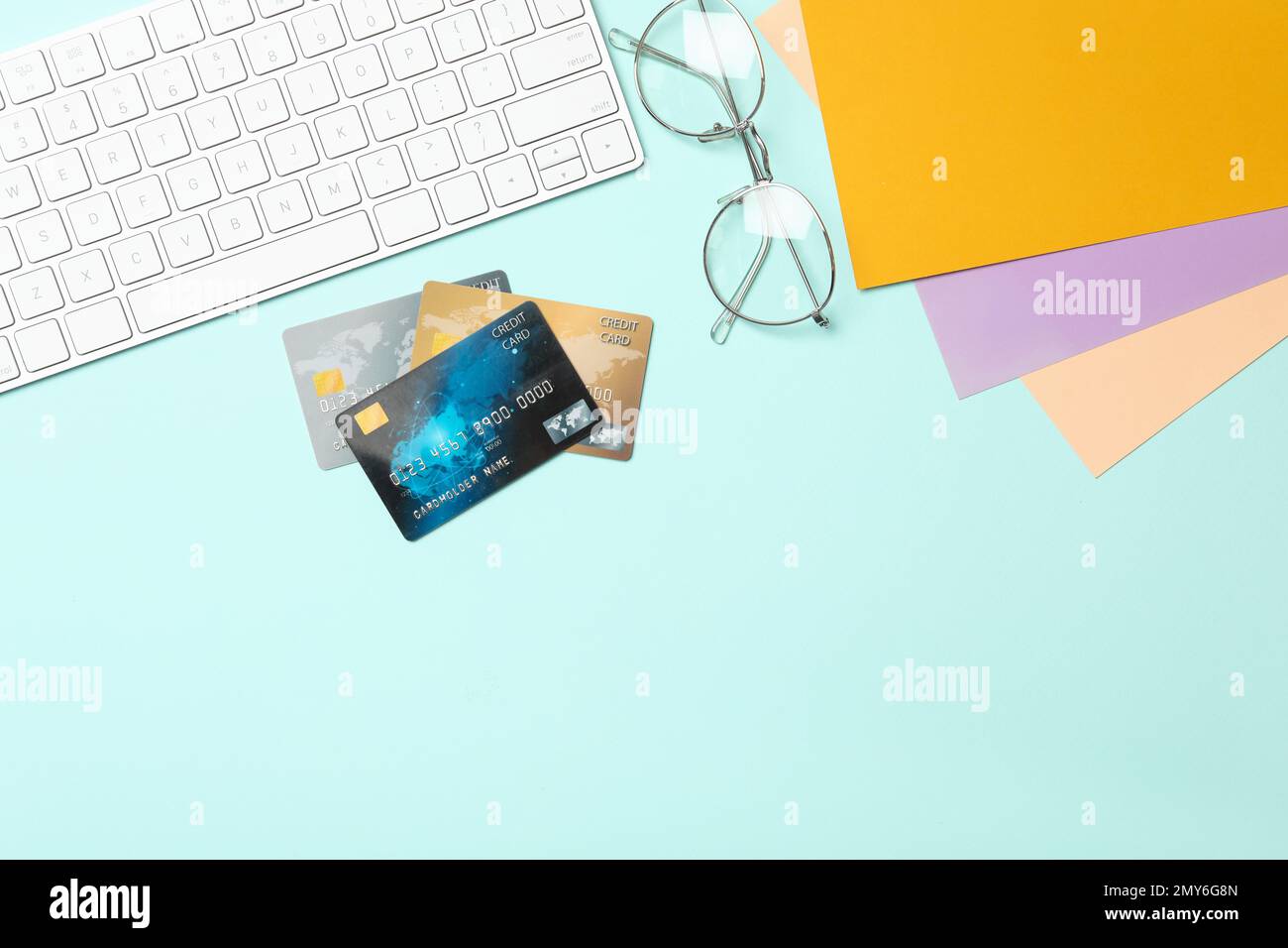Credit cards, computer keyboard and glasses on light blue background ...
