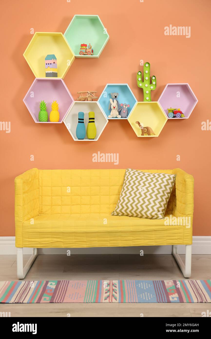 Sofa near orange wall with hexagon shaped shelves in room. Interior ...