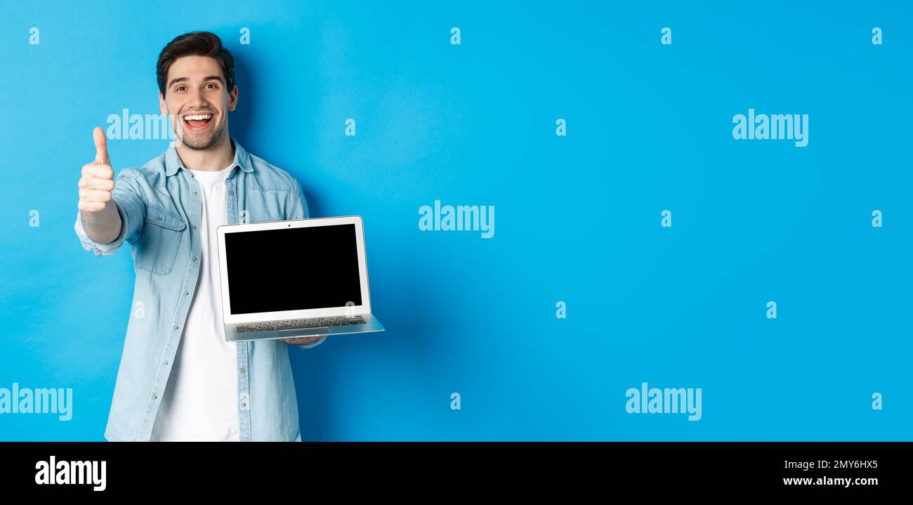 Image of satisfied handsome man showing laptop screen, thumbs-up in ...
