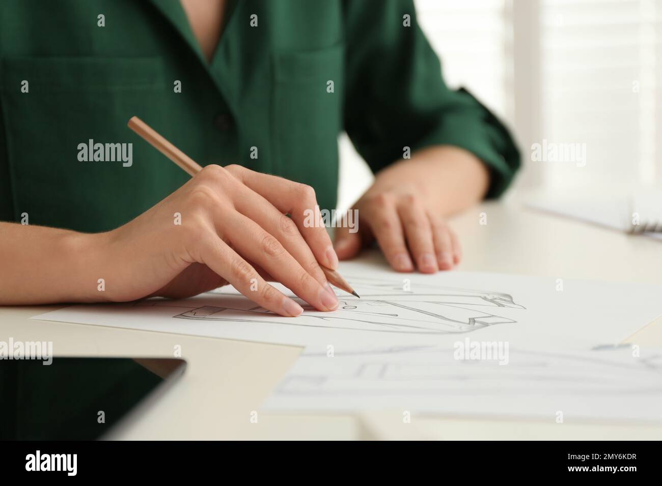 Woman drawing clothes with pencil on sheet of paper at white table ...