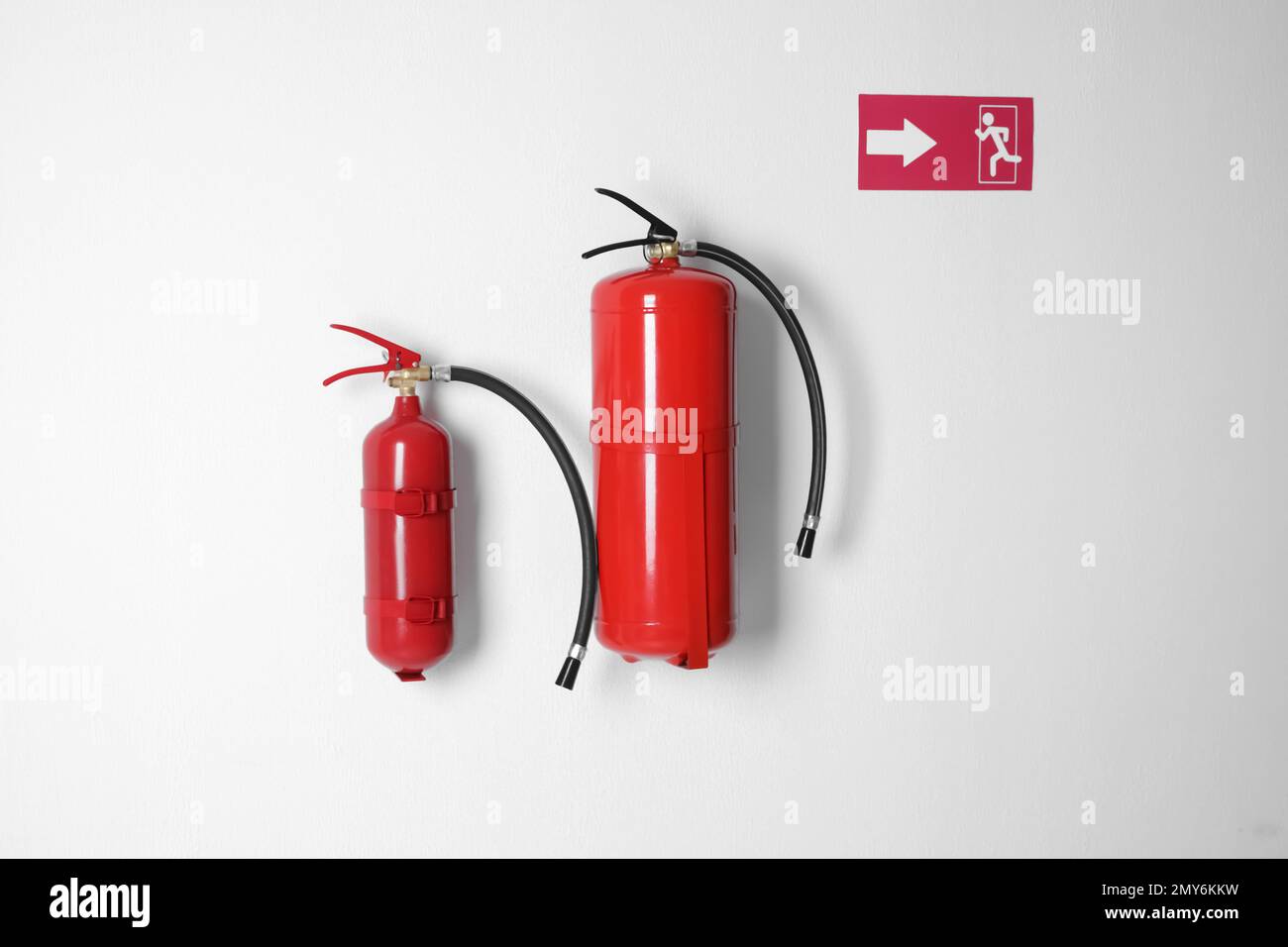 Different fire extinguishers and emergency exit sign on white wall ...