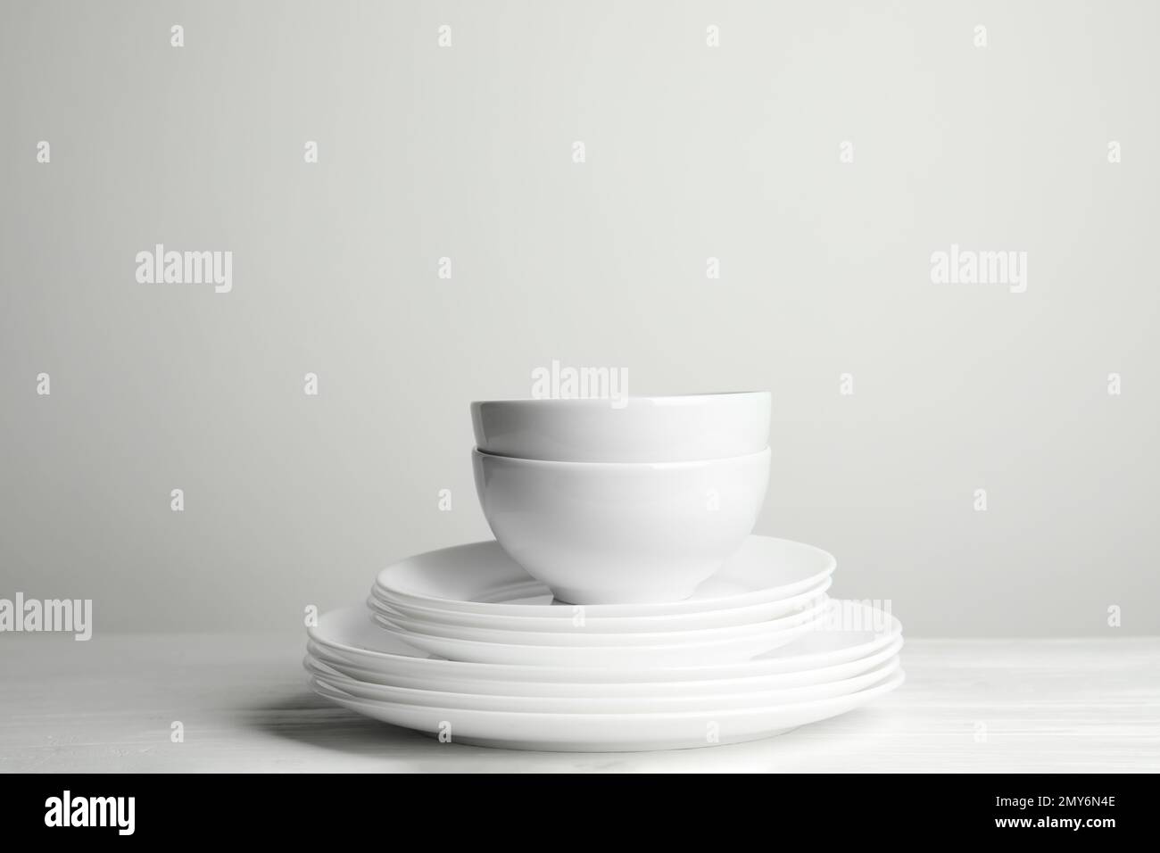 Stack of clean plates and bowls on wooden table against white ...