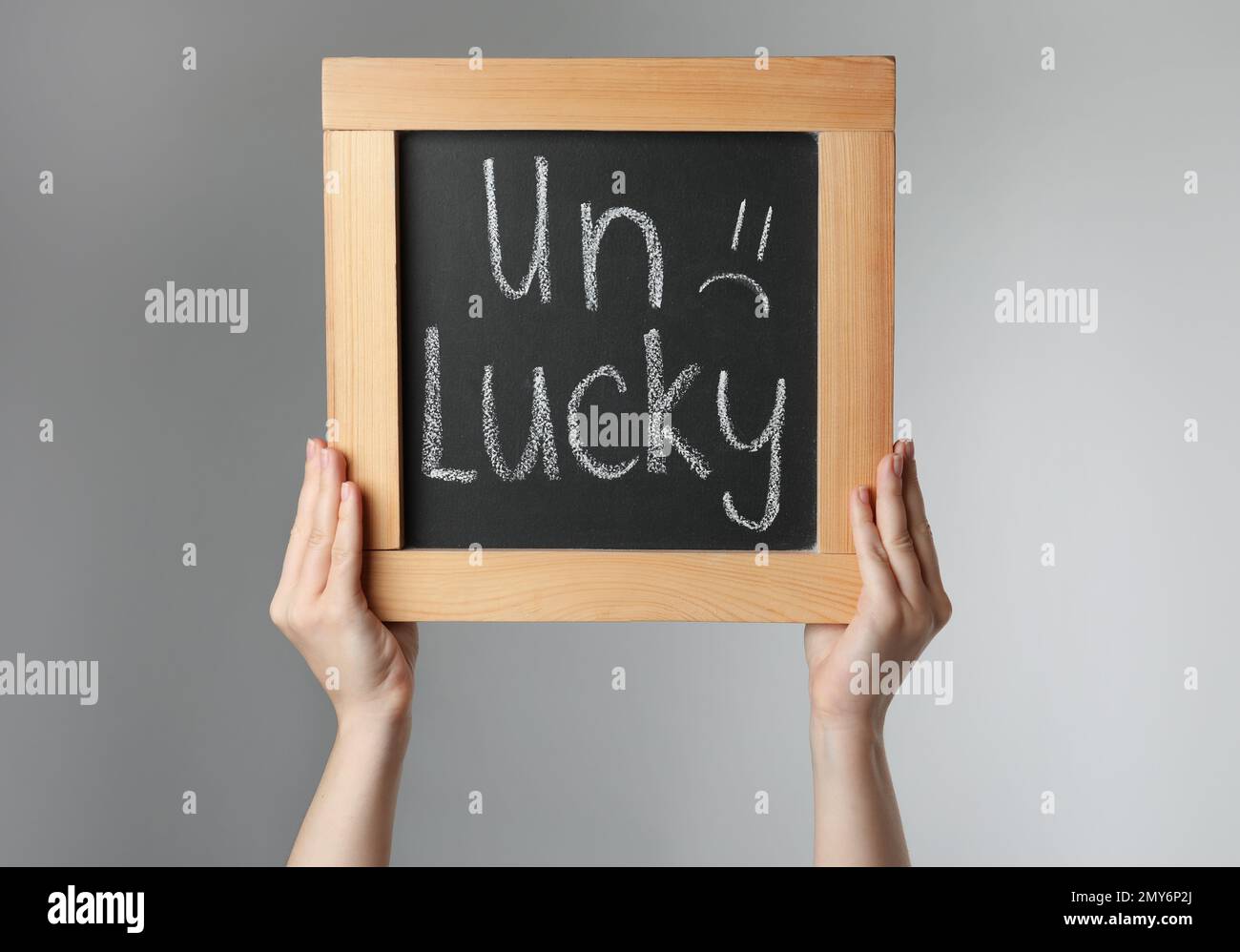 Woman holding blackboard with word UNLUCKY on light grey background ...