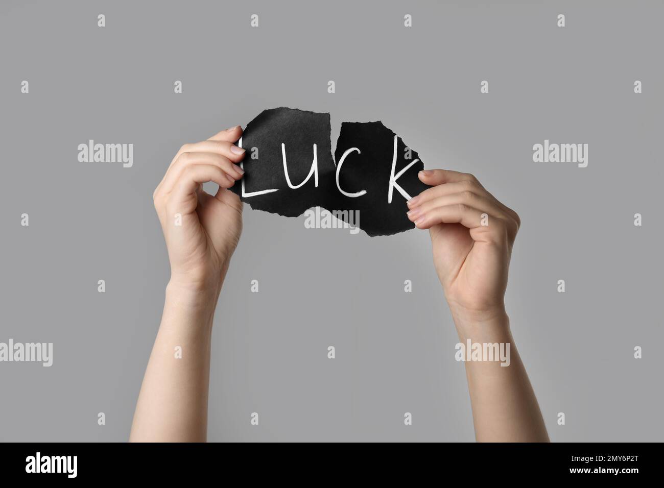 Woman tearing black paper with word LUCK on light grey background ...