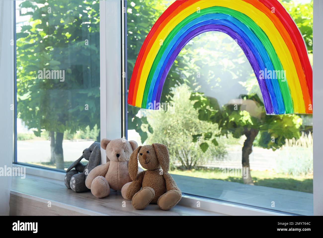 Painting of rainbow on window and toys indoors. Stay at home concept ...