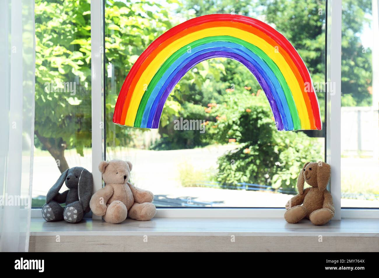 Painting of rainbow on window and toys indoors. Stay at home concept ...