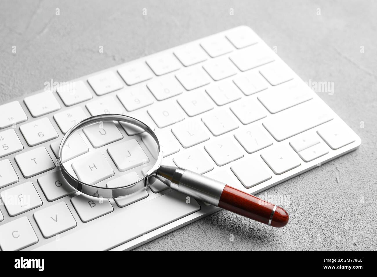 Magnifier glass and keyboard on light grey stone background, closeup ...