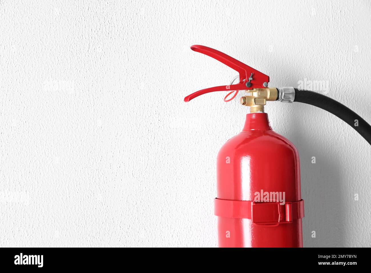 Fire extinguisher hanging on white wall, closeup. Space for text Stock ...