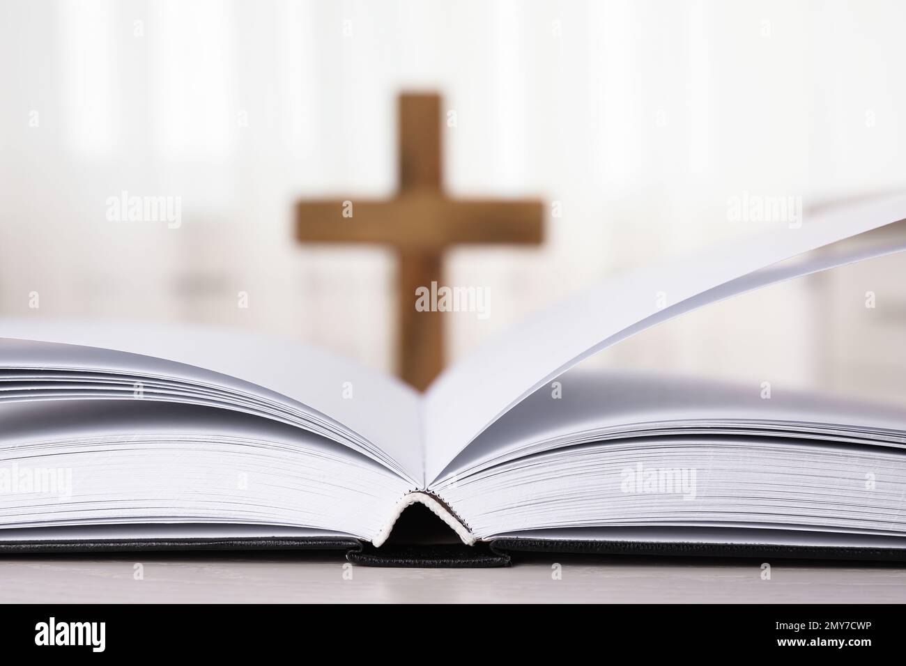 Open Bible on table and blurred cross on background, closeup. Christian ...