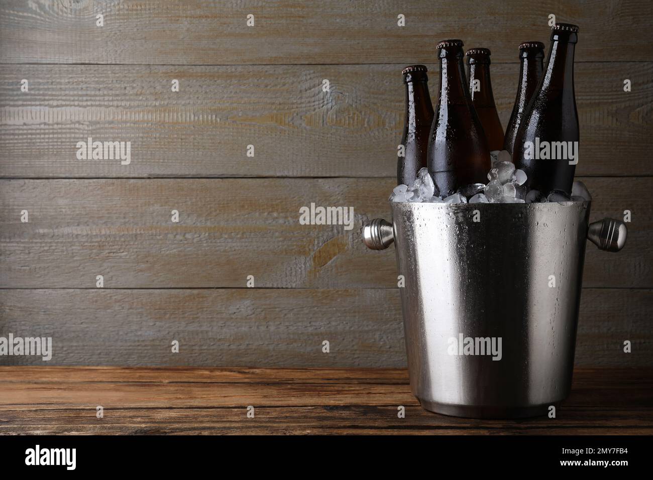 Metal bucket with beer and ice cubes on wooden table. Space for text ...