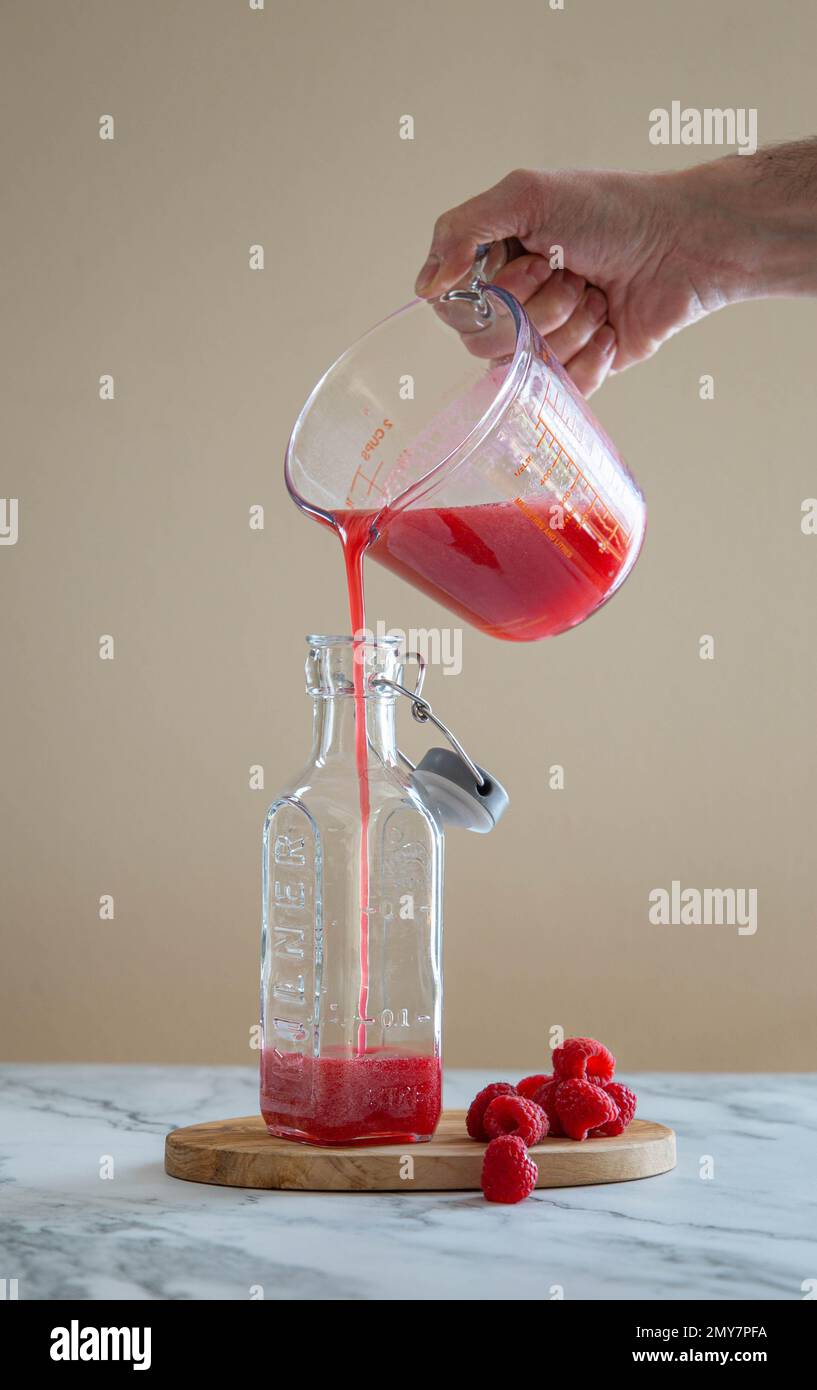 Hand pouring a red liquid on a cristal bottle with raspberries on the ...