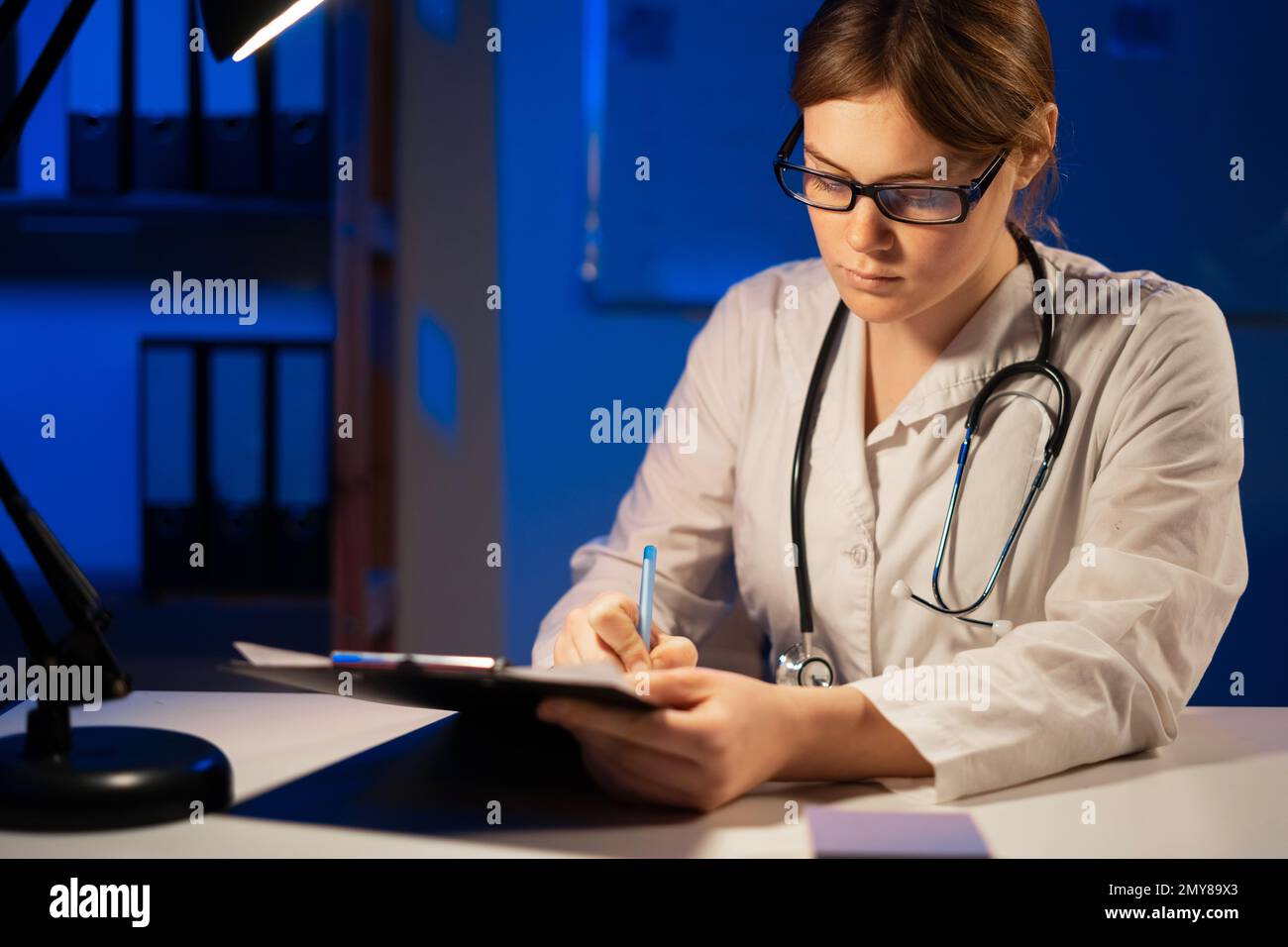 Female GP making notes with pen while receiving visitor close-up in ...