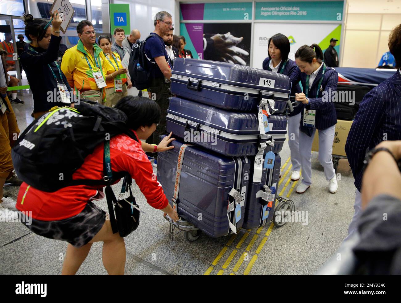 Members of the Japanese Olympic delegation guide a cart full of luggage ...