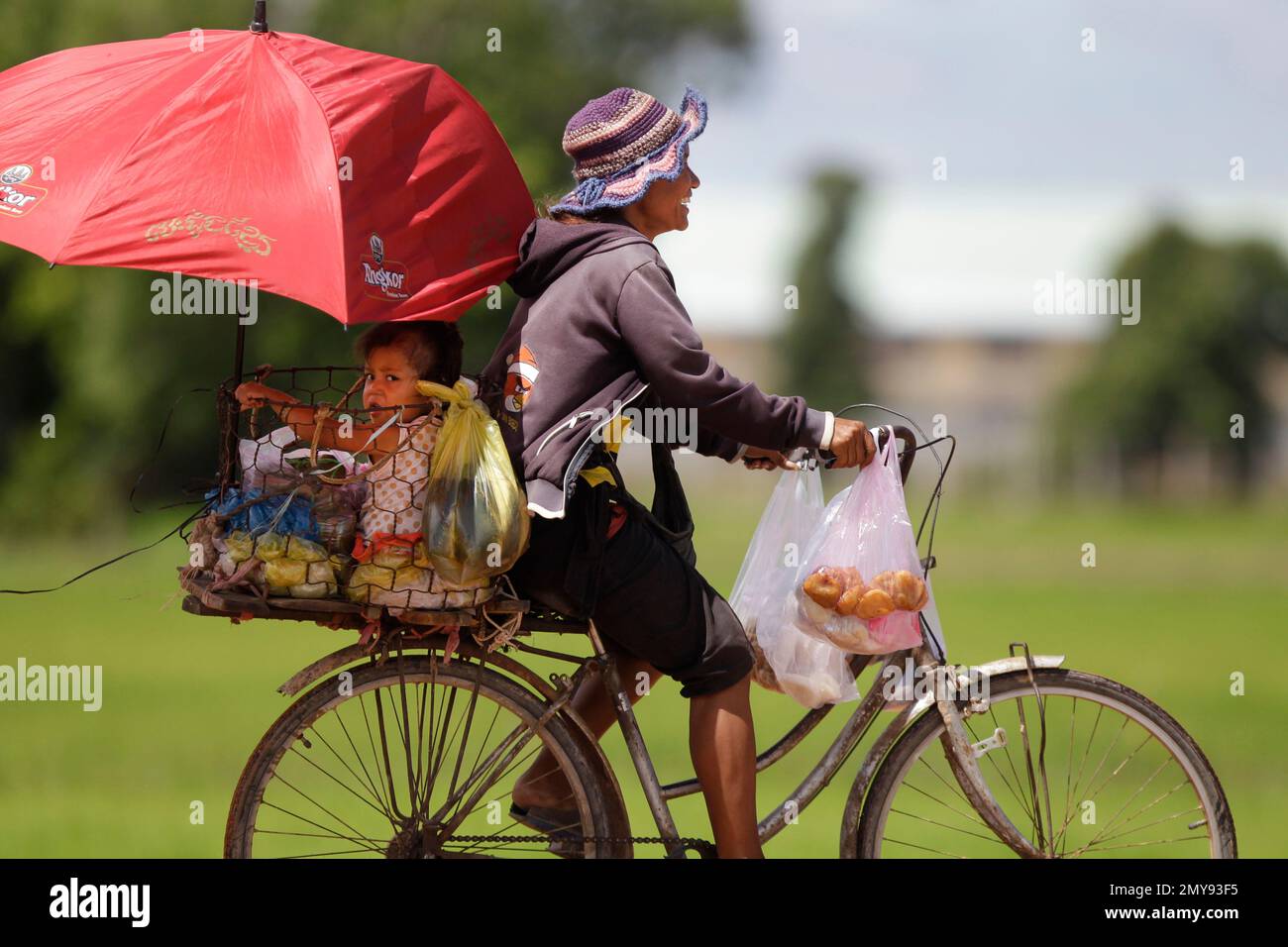 A Cambodian vendor, right, carries her child on a bicycle's back seat ...