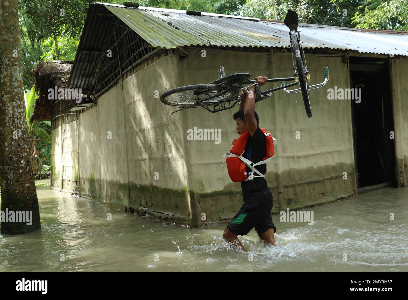 A rescuer walks carrying a bicycle recovered from flood affected house ...