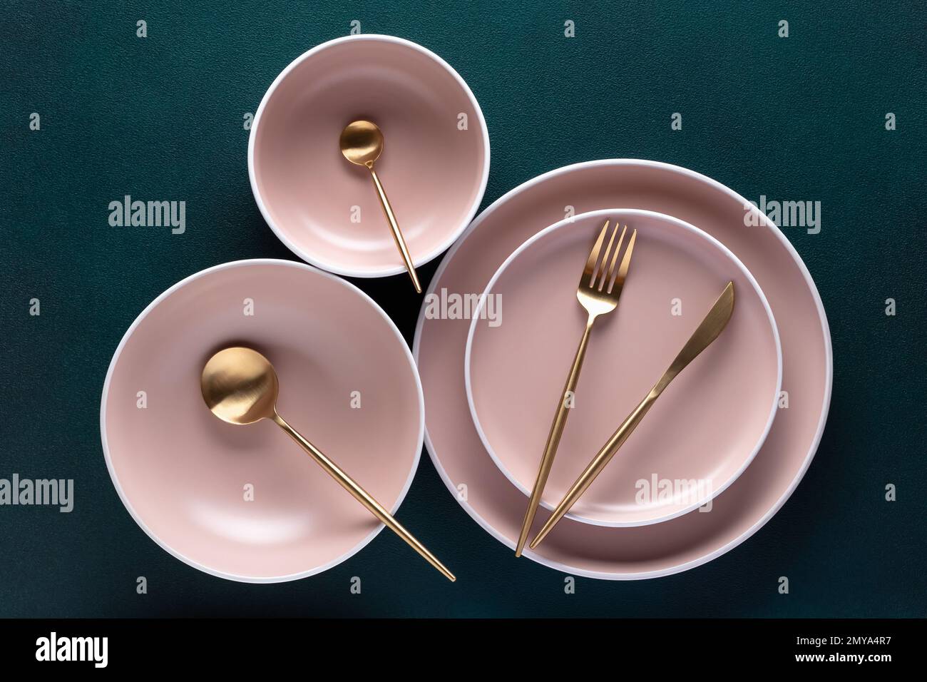 Crockery and golden cutlery on a dark green background, table top view ...