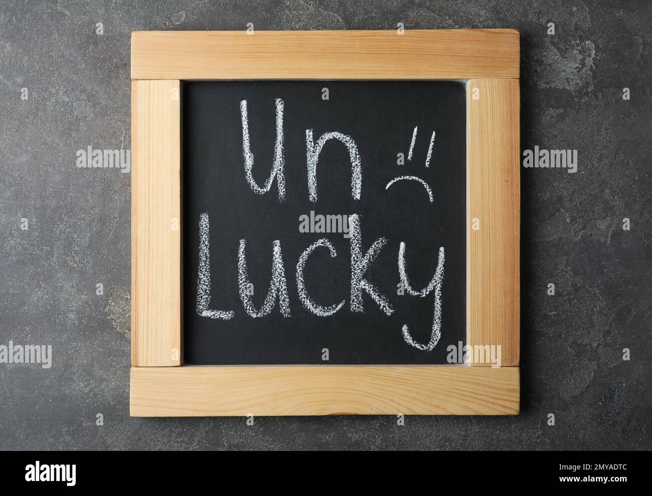 Blackboard with word UNLUCKY and sad face on grey stone background, top ...