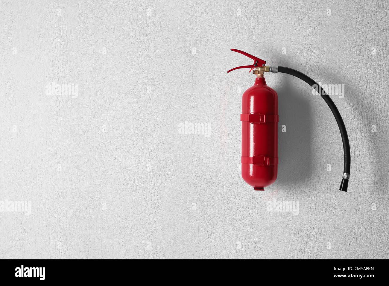 Fire extinguisher hanging on white wall. Space for text Stock Photo - Alamy