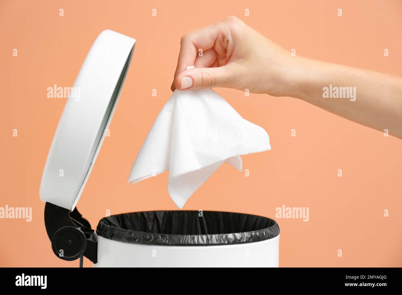 Woman putting paper tissue into trash bin on light brown background ...