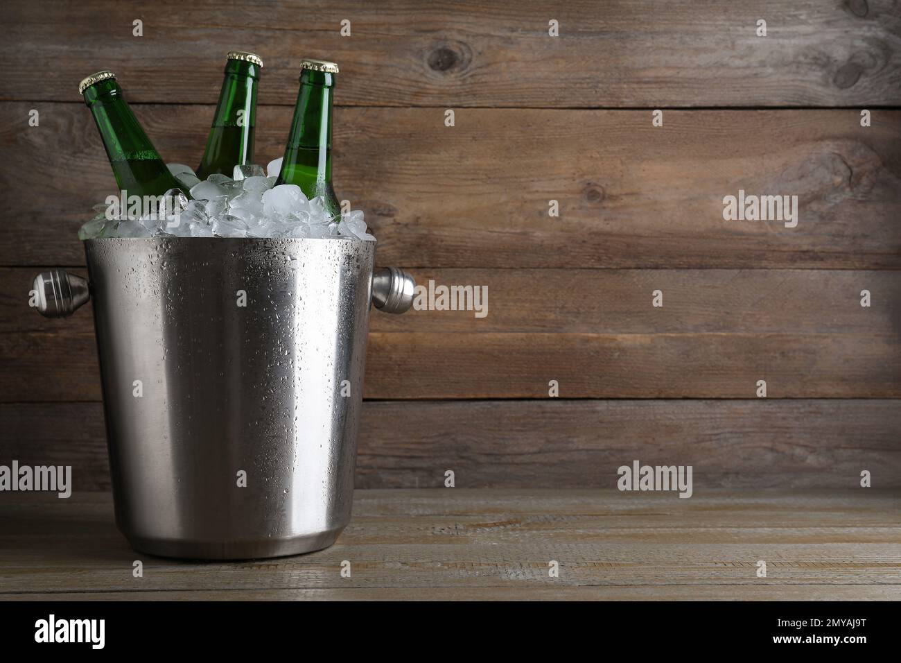 Metal bucket with beer and ice cubes on wooden table. Space for text ...