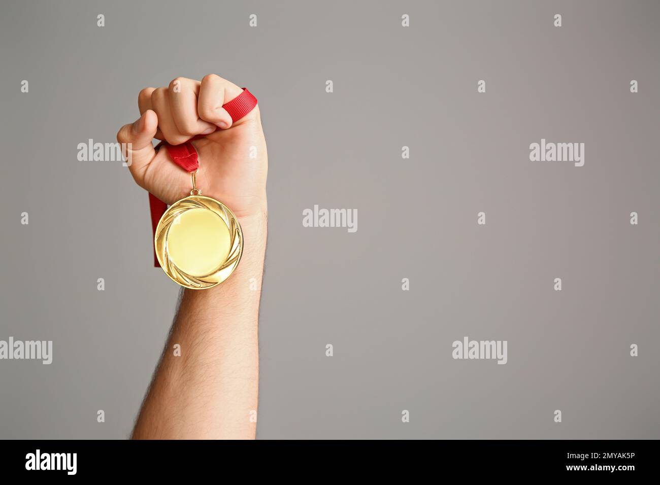 Man holding golden medal on grey background, closeup. Space for design ...