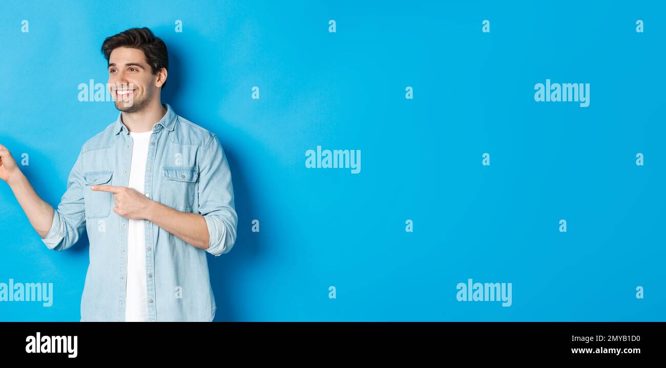 Handsome adult man introduce product, looking and pointing fingers left ...