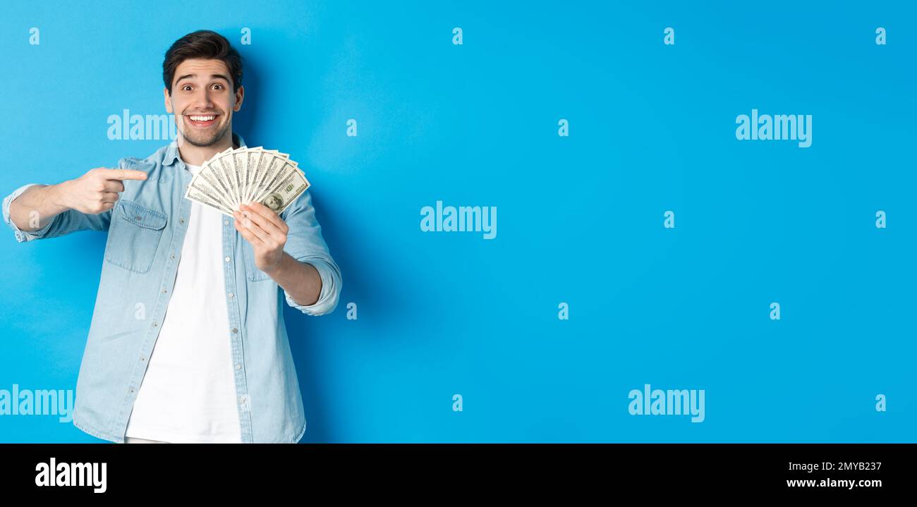 Surprised smiling man in casual clothes, pointing fingers at money ...