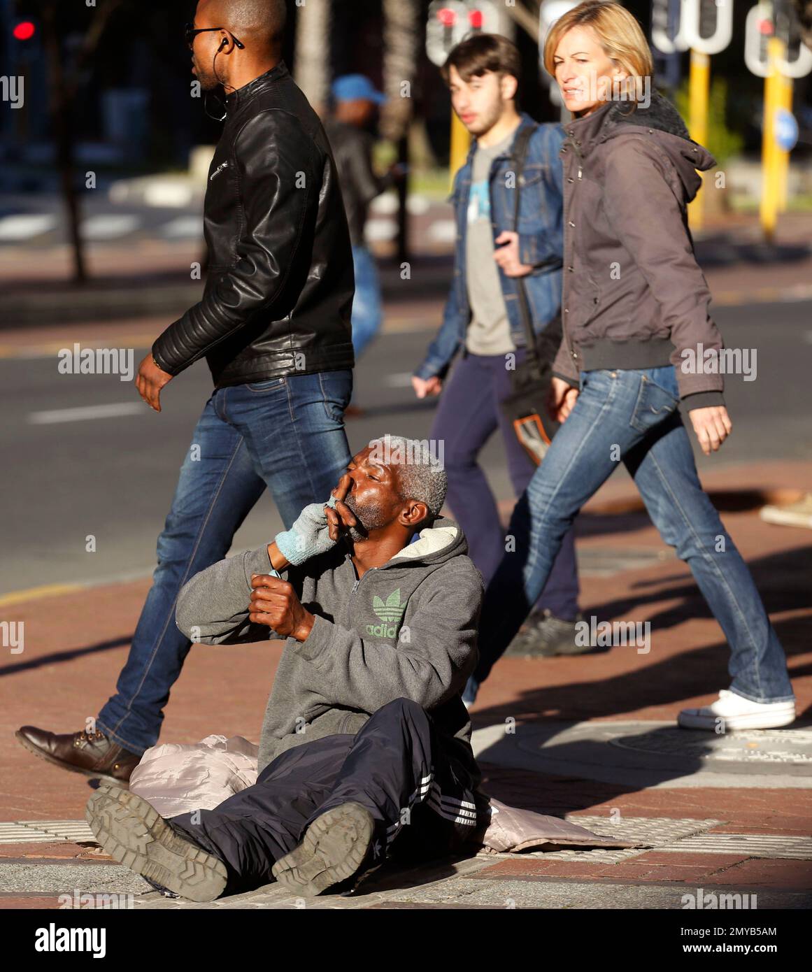 A destitute man, center, holds his hand near his mouth after he fell ...