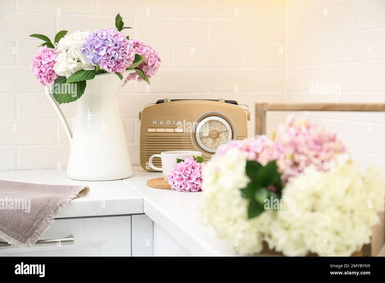 Beautiful hydrangea flowers, cup and radio set on light countertop ...