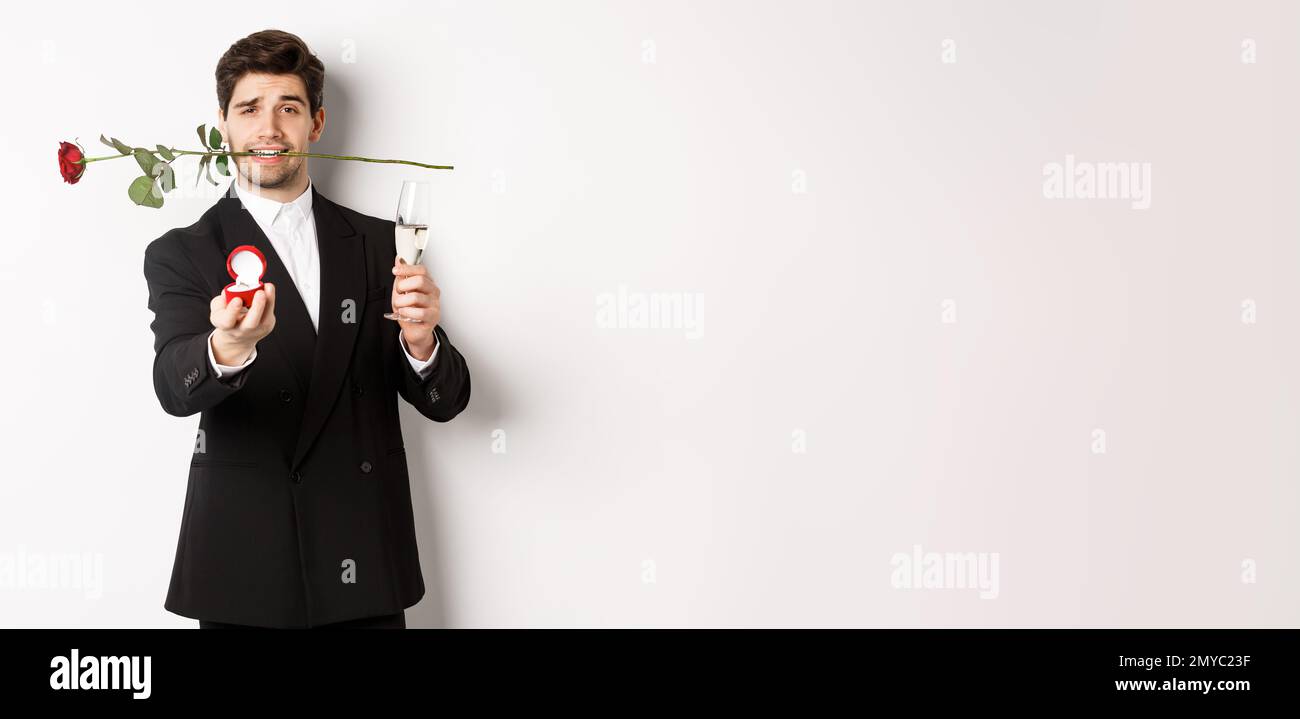 Romantic young man in suit making a proposal, holding rose in teeth and ...