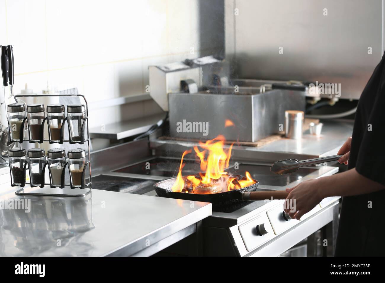 Female chef cooking meat with burning flame on stove in restaurant ...