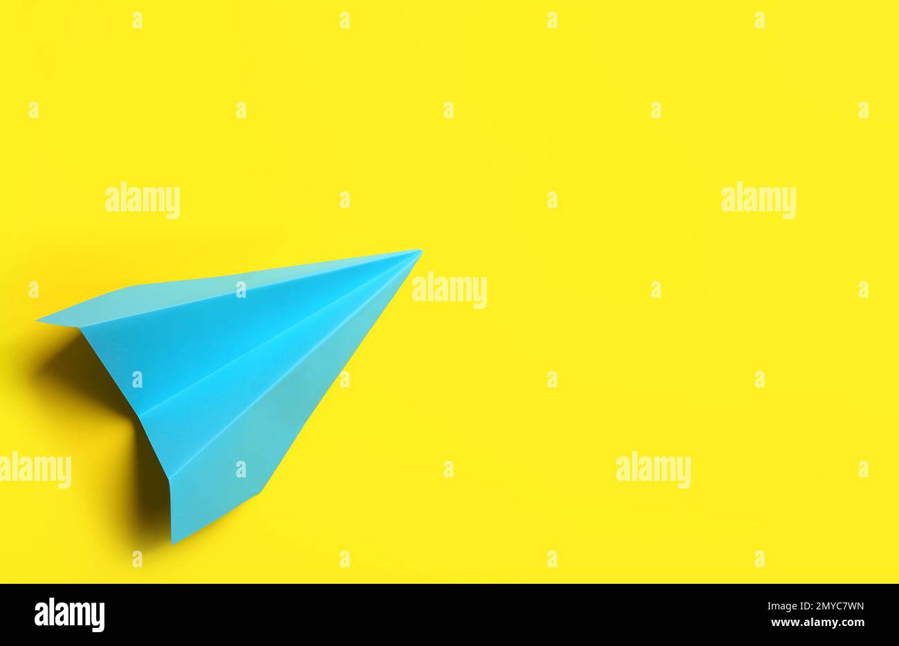 Light blue paper plane on yellow background, top view. Space for text ...