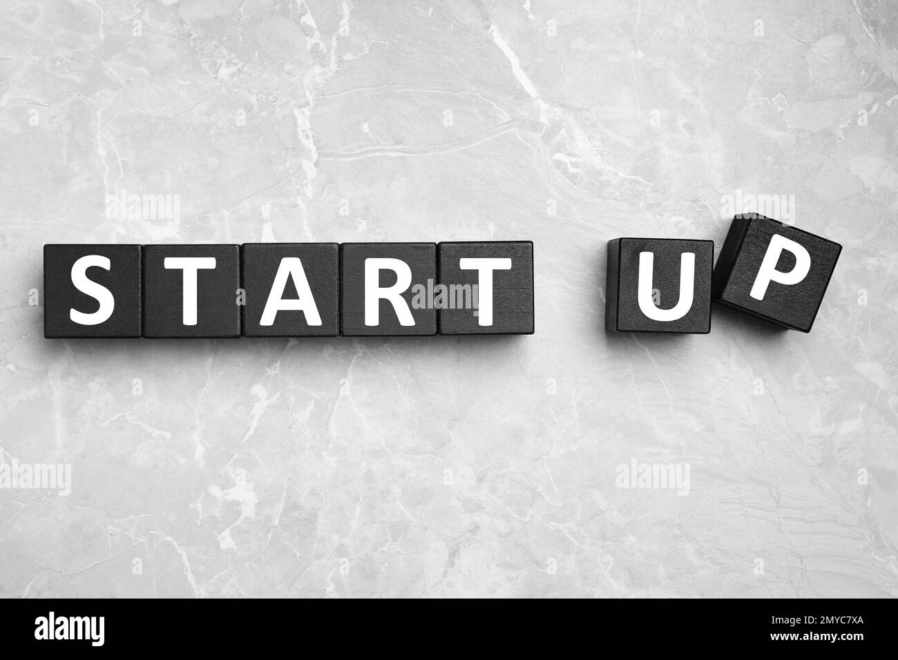 Words START UP made with black cubes on light grey marble background ...