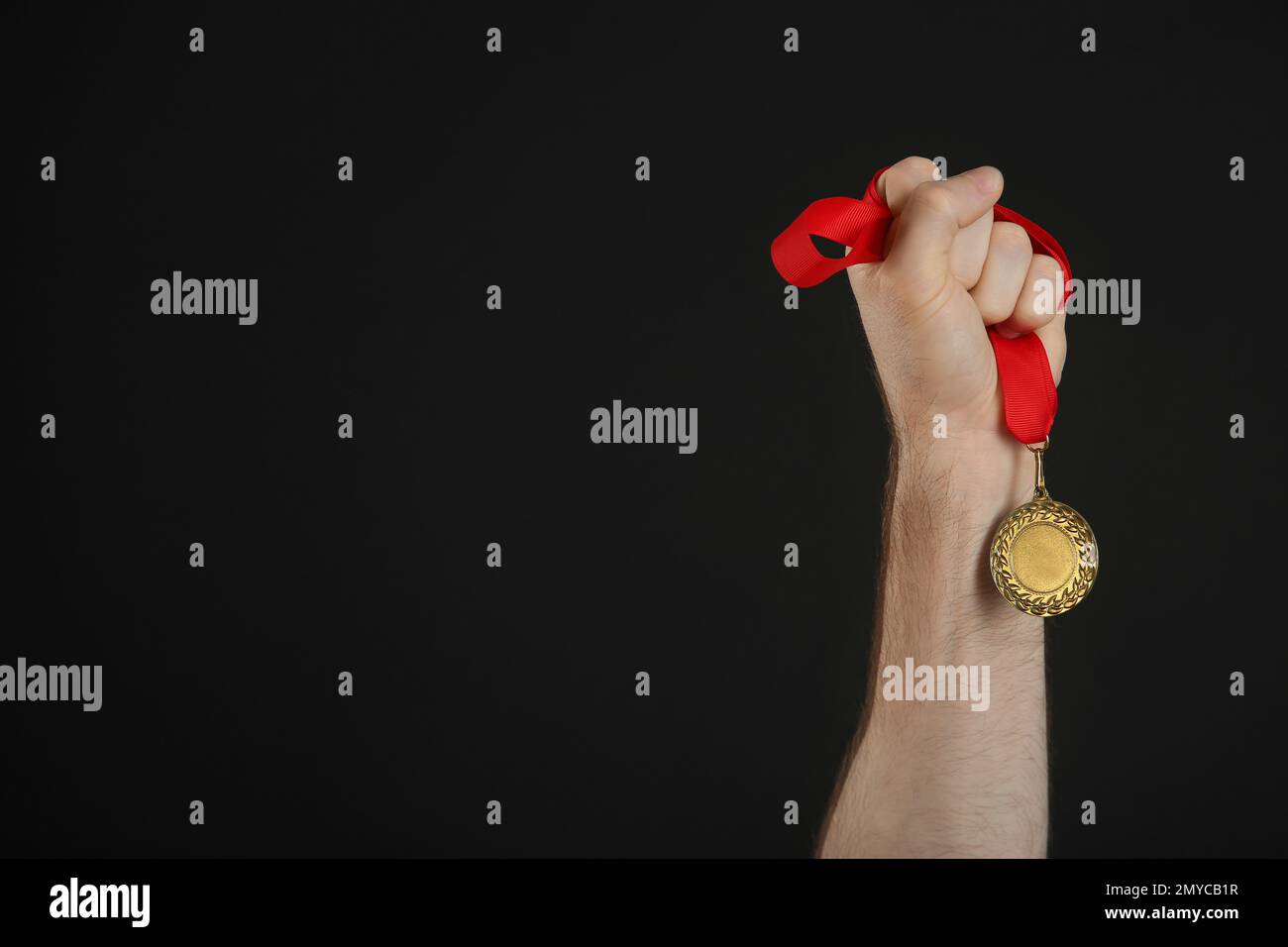 Man holding golden medal on black background, closeup. Space for design ...