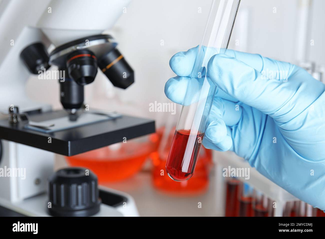 Scientist holding test tube with blood sample near microscope, closeup ...