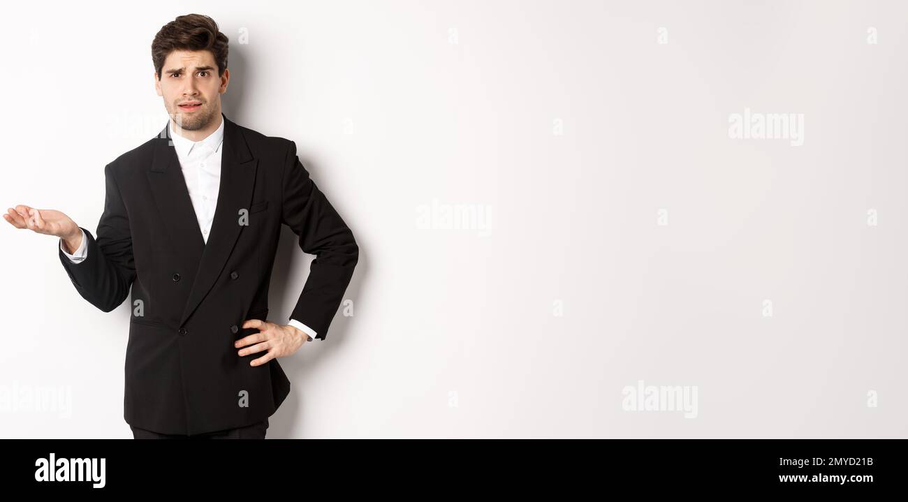 Image of confused handsome man in formal suit, raising hand and ...
