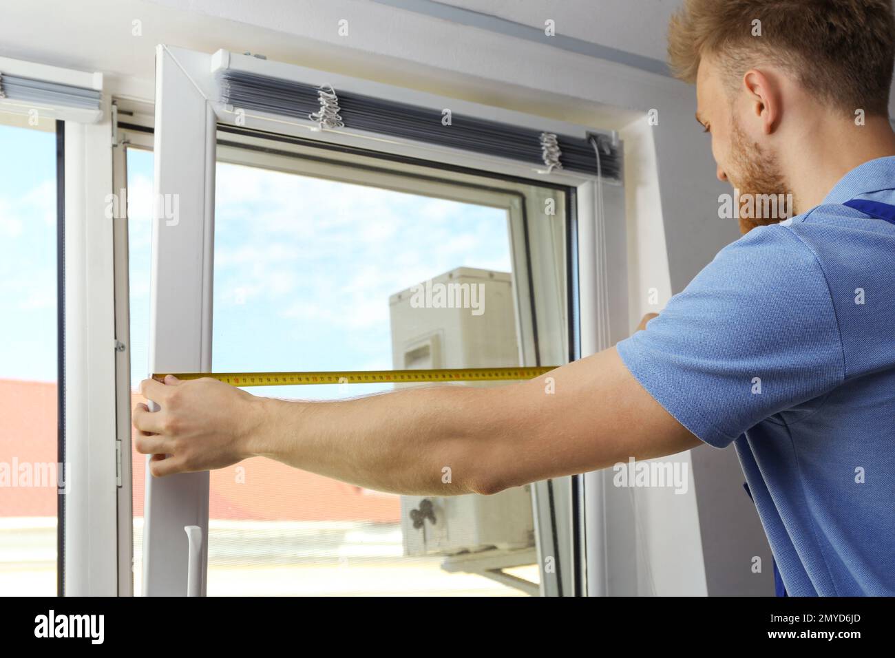 Handyman with tape measure installing window blinds indoors Stock Photo ...