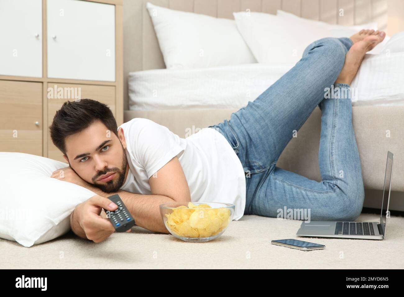 Lazy young man with bowl of chips watching TV while lying on floor at ...