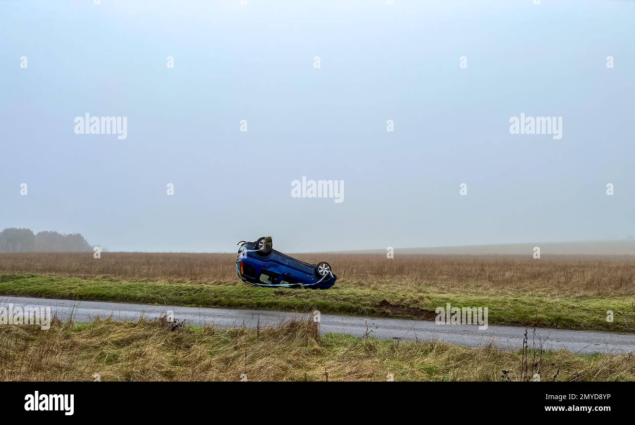an overturned blue Suzuki hatchback car resting on its roof having ...