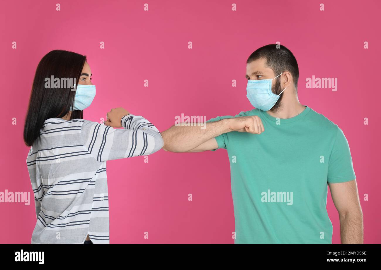Man and woman bumping elbows to say hello on pink background. Keeping ...
